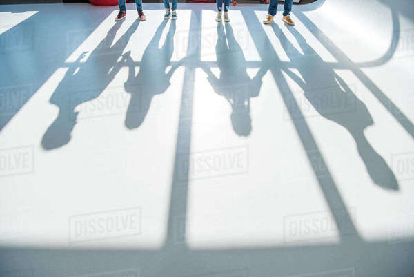 Cropped shot of young people standing together and shadows on grey ...