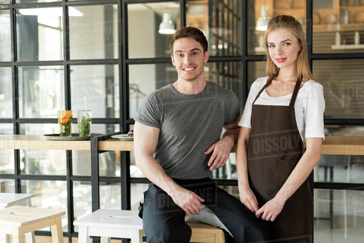 Portrait of young waiter and waitress looking at camera in cafe ...