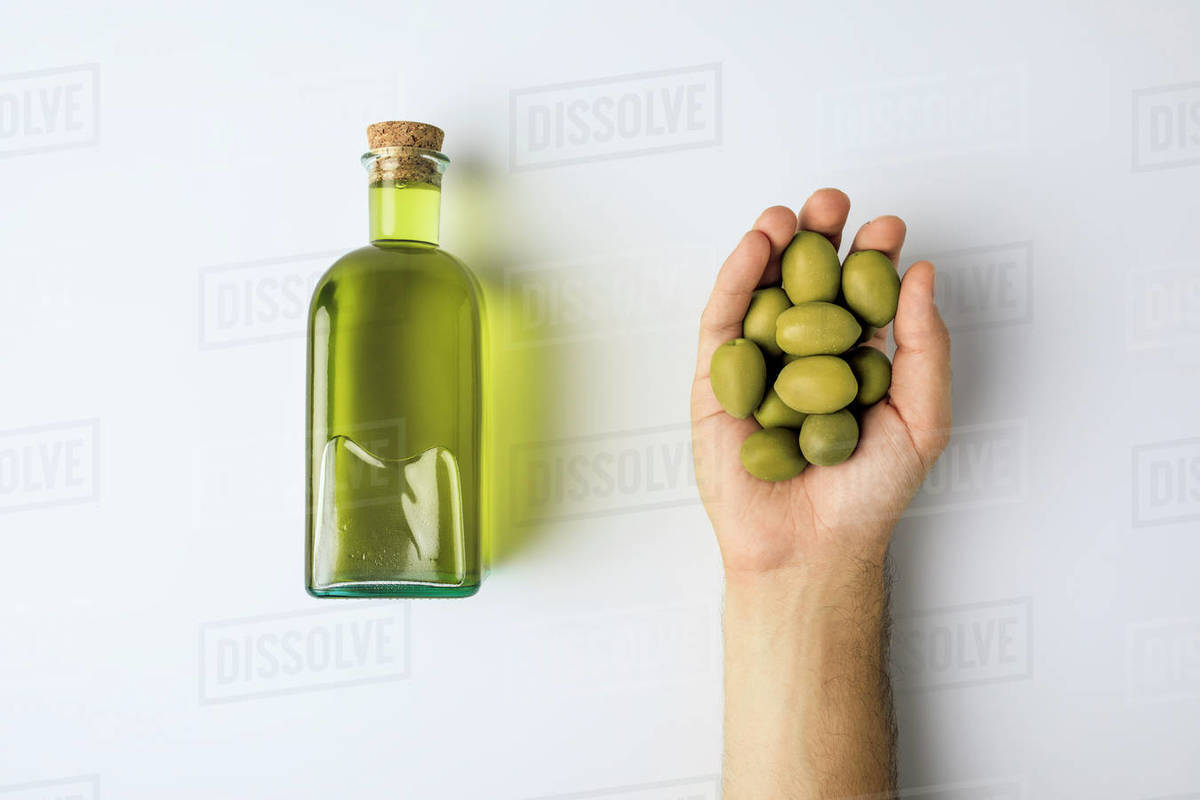 Cropped image of man holding green olives in hand and bottle of olive ...