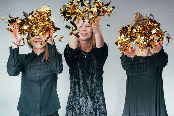 Group of young women throwing up golden confetti, isolated on grey ...