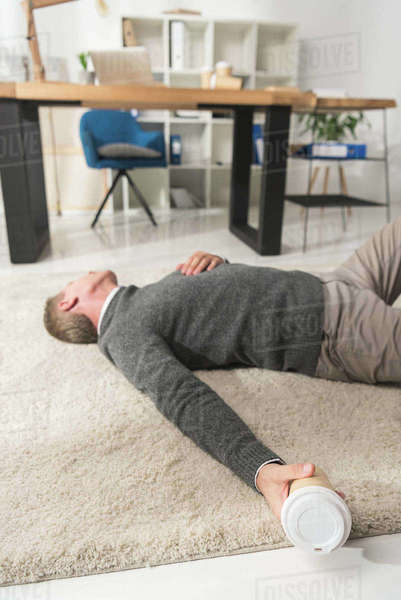 unconscious man lying on a floor in office and holding disposable ...
