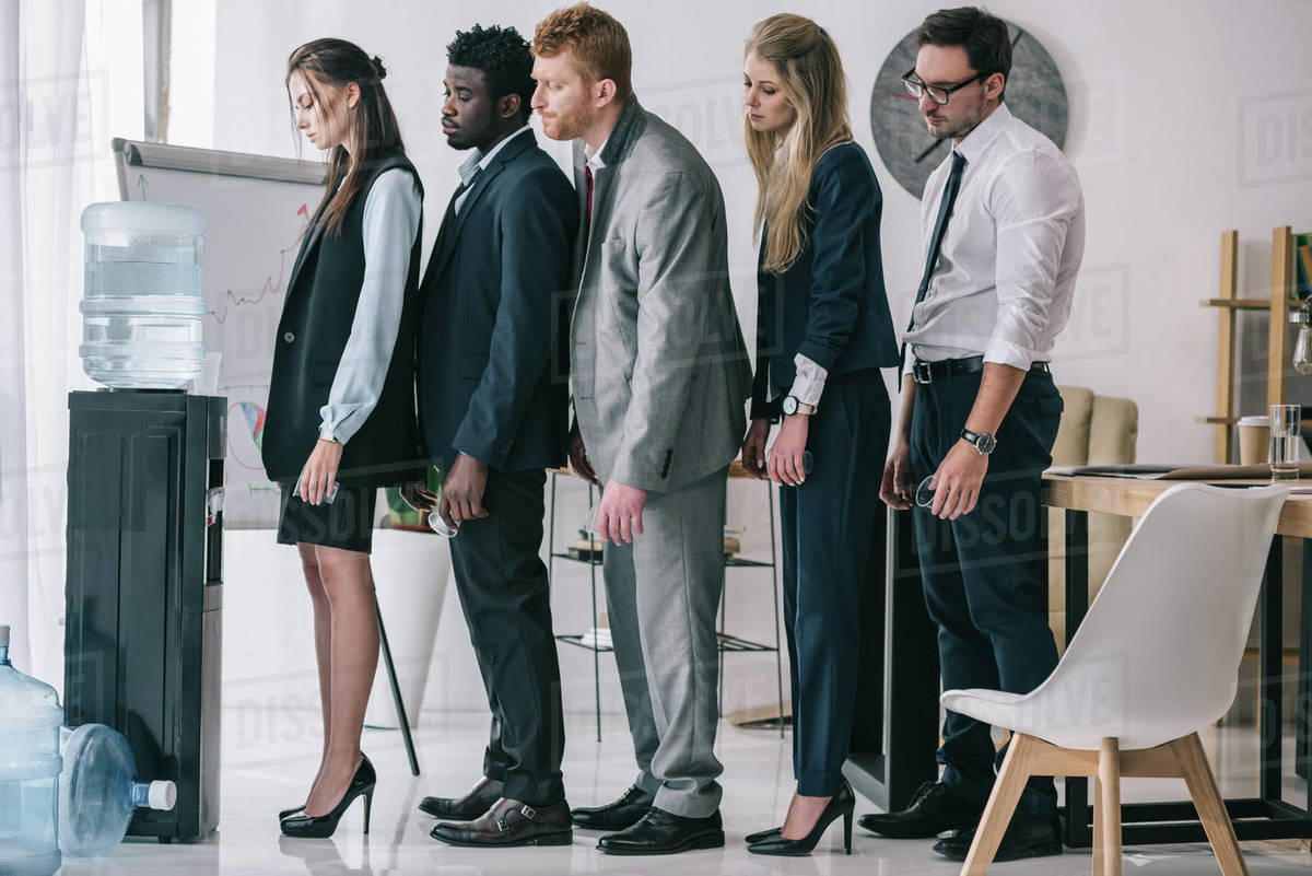 side view of business colleagues standing in queue for water dispenser ...