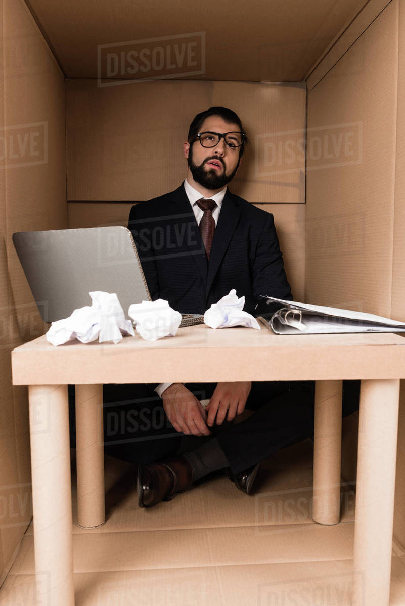 Exhausted businessman sitting in box with cardboard laptop and ...