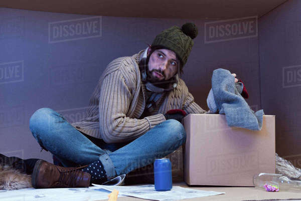 Homeless man sitting in cardboard box with clothes - Stock Photo - Dissolve