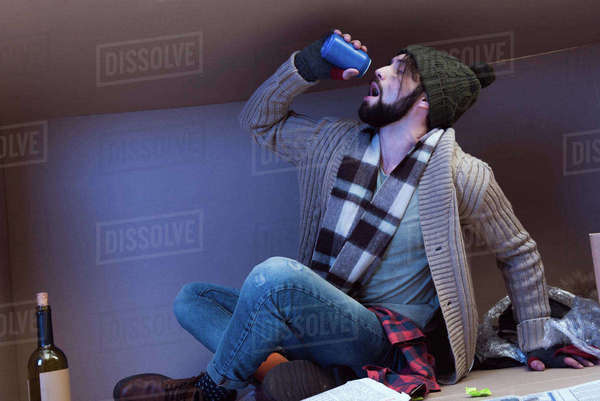 Homeless man drinking alcohol while sitting in big cardboard box ...