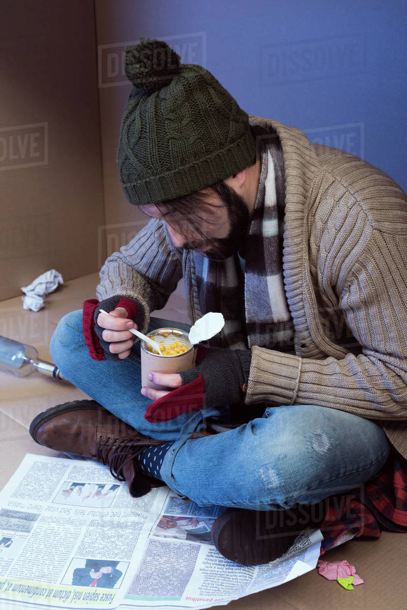 Muddy homeless man eating canned food in cardboard box - Royalty-free ...
