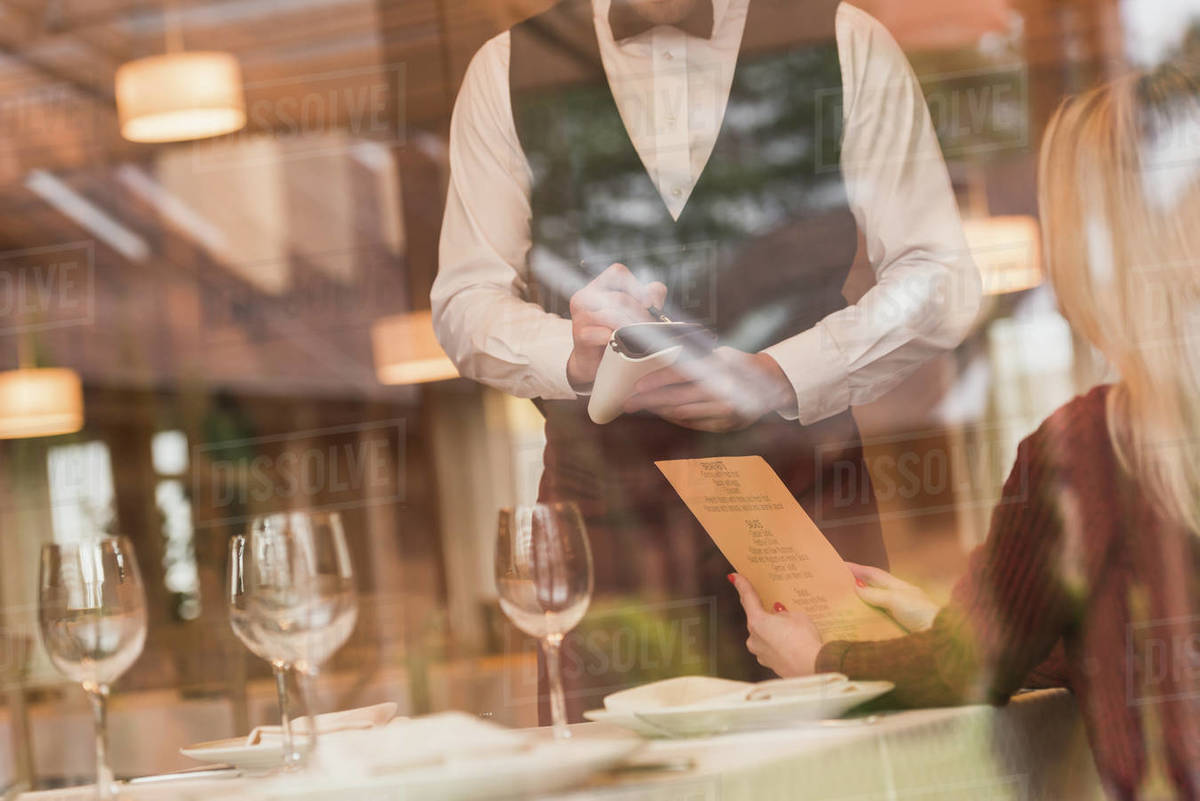 Cropped image through window of Waiter writing down the order of ...