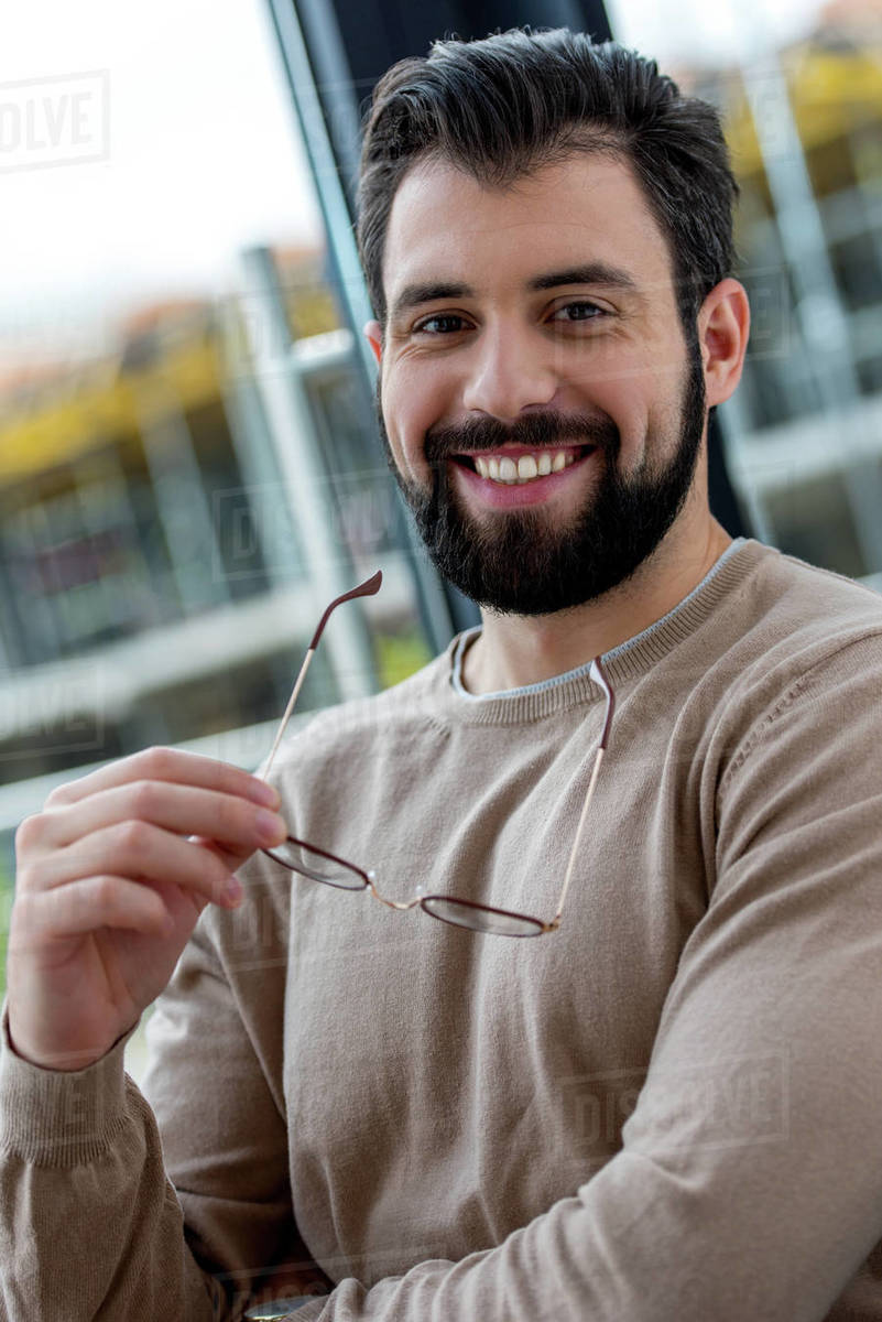 Portrait of smiling handsome man holding glasses in hand and looking at ...