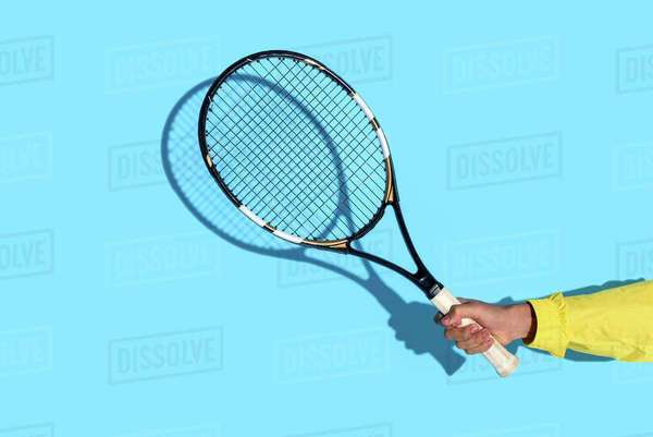 Close-up view of male hand holding tennis racket on blue background ...