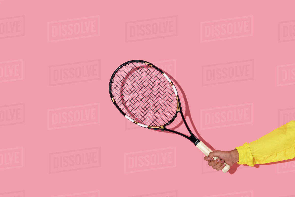 Close-up view of male hand holding tennis racket on pink background ...