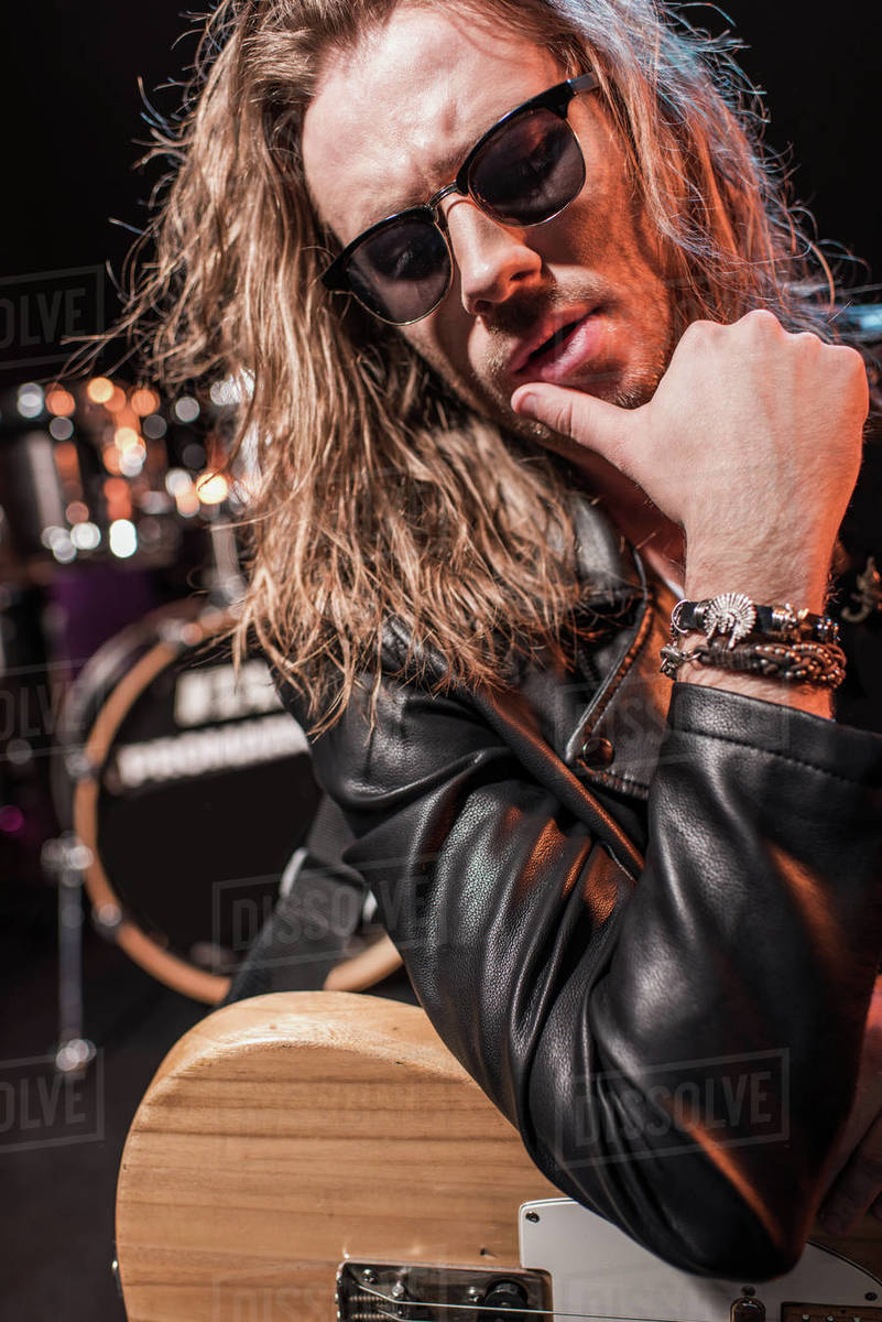 Handsome rock star in eyeglasses posing with electric guitar on stage ...