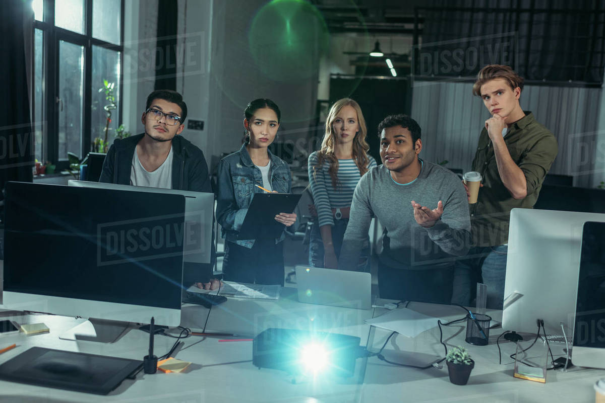 Young people watching presentation in modern office at nighttime ...
