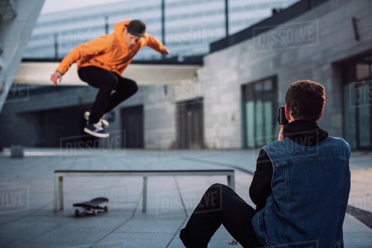 Man taking photo of skateboarder jumping over bench - Stock Photo ...