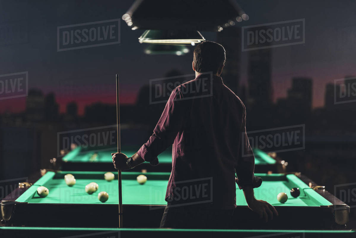 Back view of successful man standing beside pool table with at bar ...