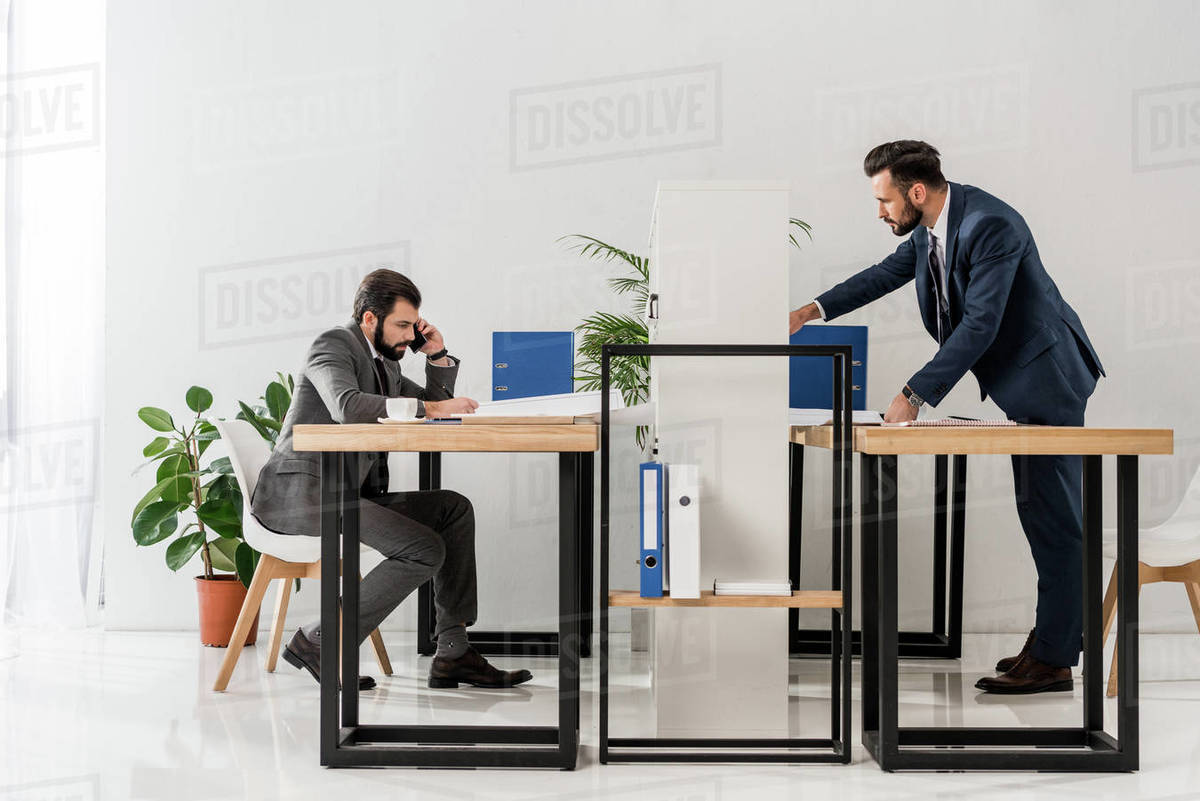 Side view of businessmen working at tables in office - Stock Photo ...
