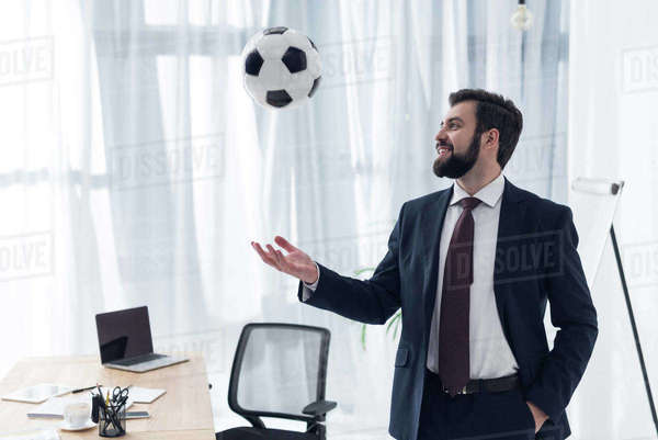 Portrait of smiling businessman playing with soccer ball at workplace ...