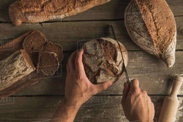Partial top view of person cutting loaf of bread with knife - Royalty ...