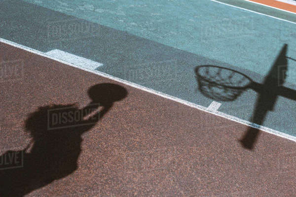 Shadows of female figure throwing ball into basket on ground of sports ...