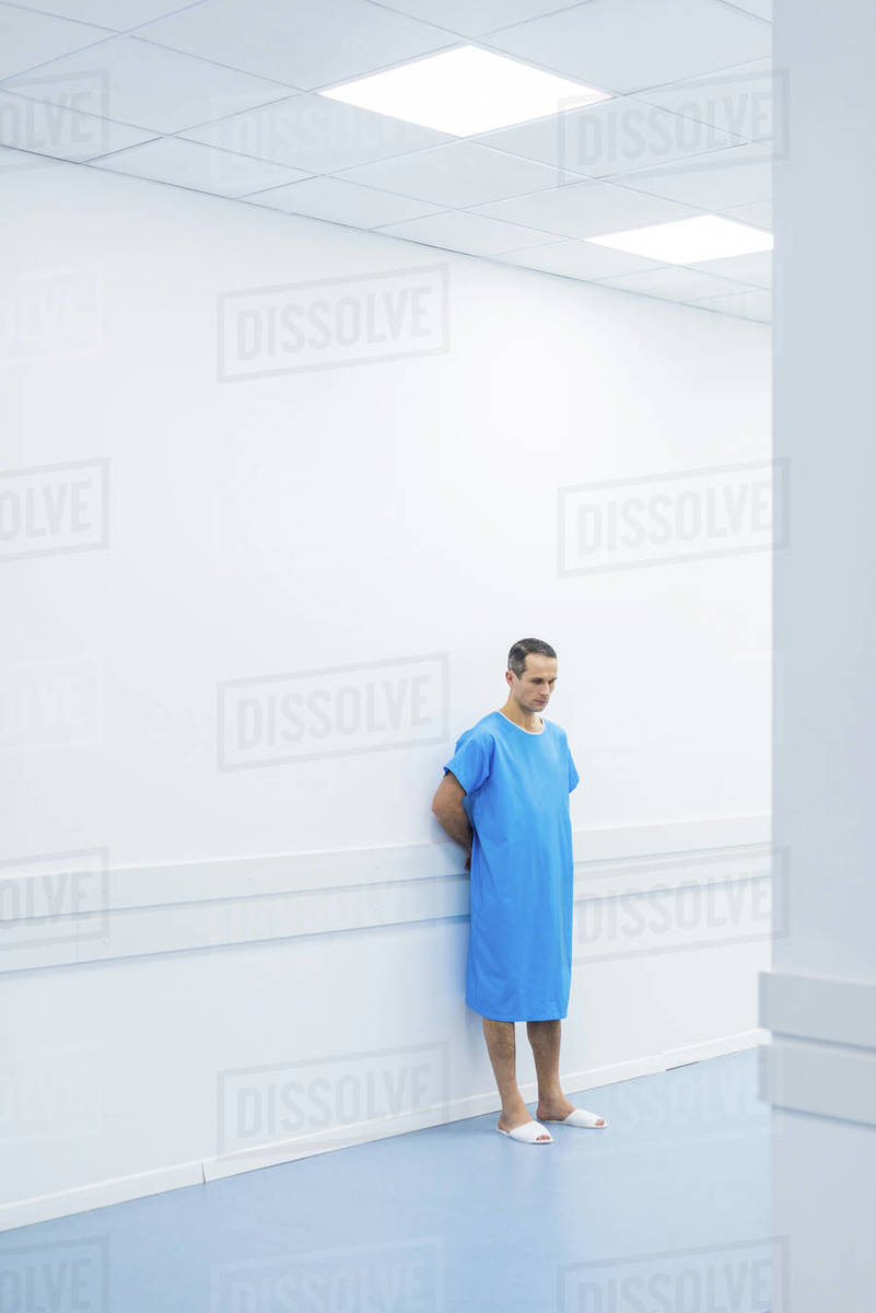 male patient in medical gown standing at wall in hospital - Royalty ...