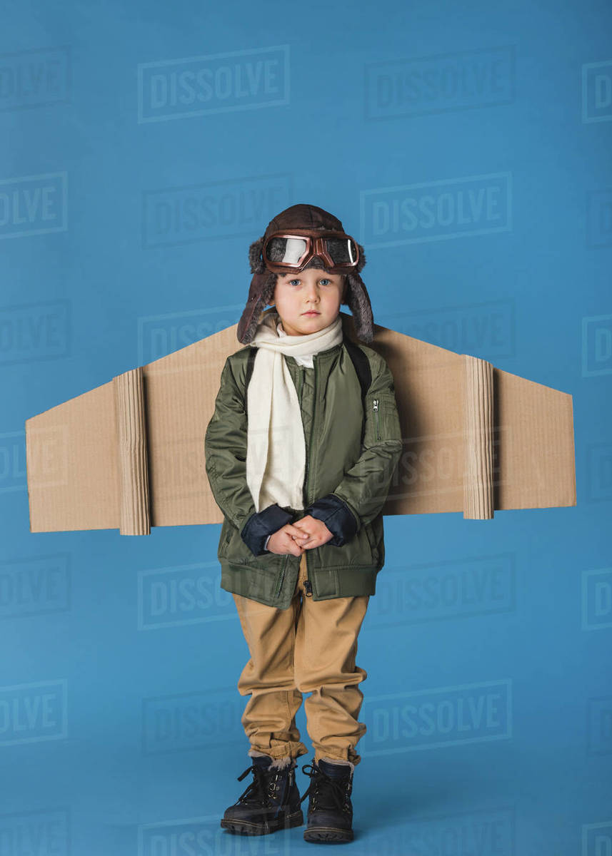 cute little boy in pilot costume with paper plane wing isolated on blue ...
