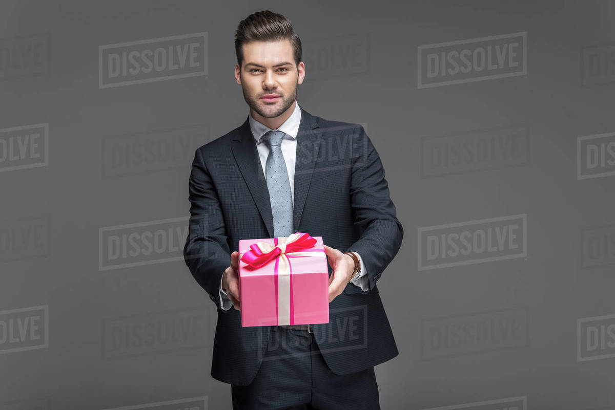 handsome man in suit holding present, isolated on grey - Stock Photo ...