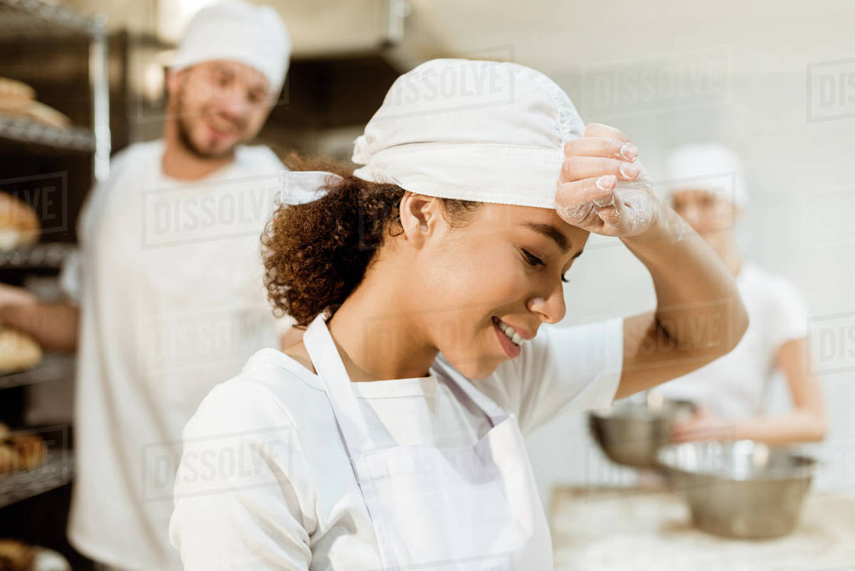 Happy and exhausted female baker working at baking manufacture while ...