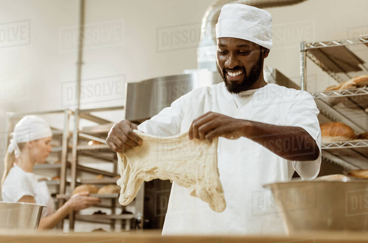 Happy handsome african american baker preparing dough on baking ...