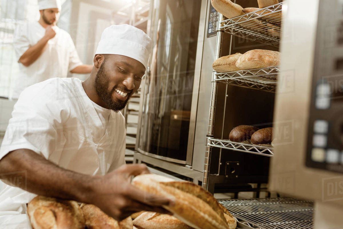 Happy african american baker with tray of fresh loaves of bread on ...