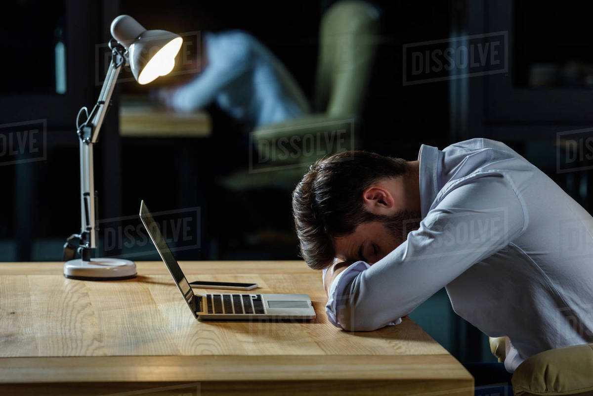 Side view of tired businessman sleeping at table with laptop - Royalty ...