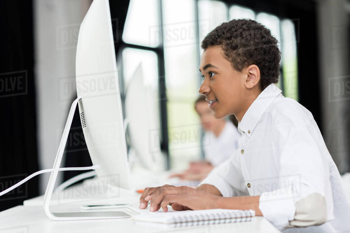 Side view of African American teen boy typing on keyboard in front of ...