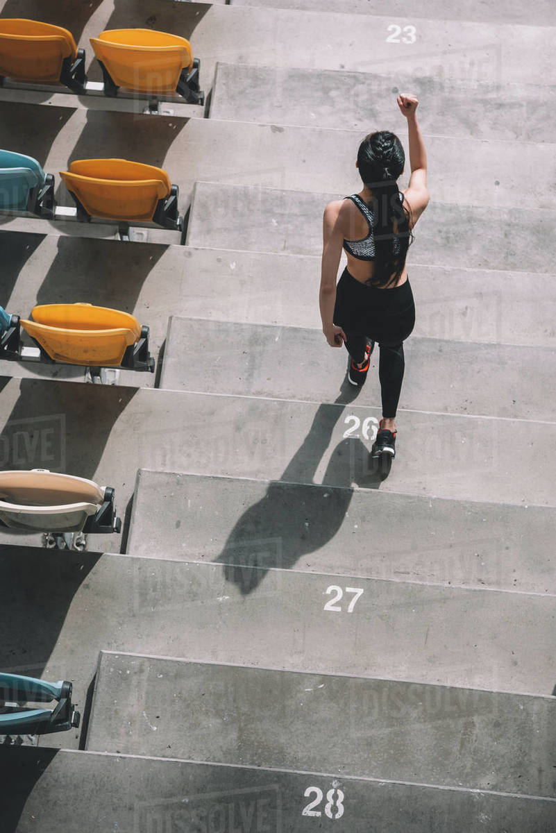 Elevated view of sportswoman running on stadium stairs, young girl ...