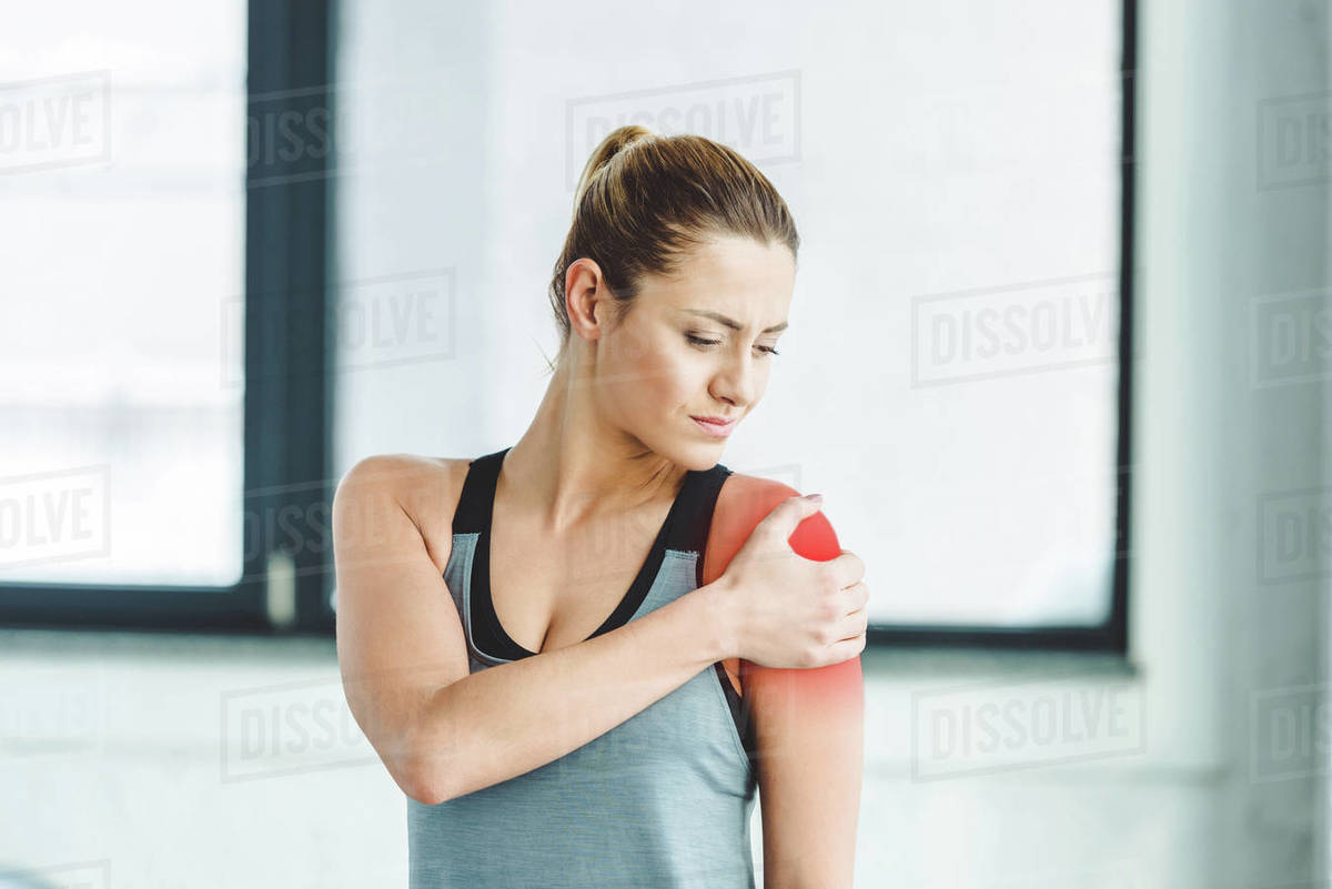Portrait of young sportswoman suffering from pain in arm at gym ...