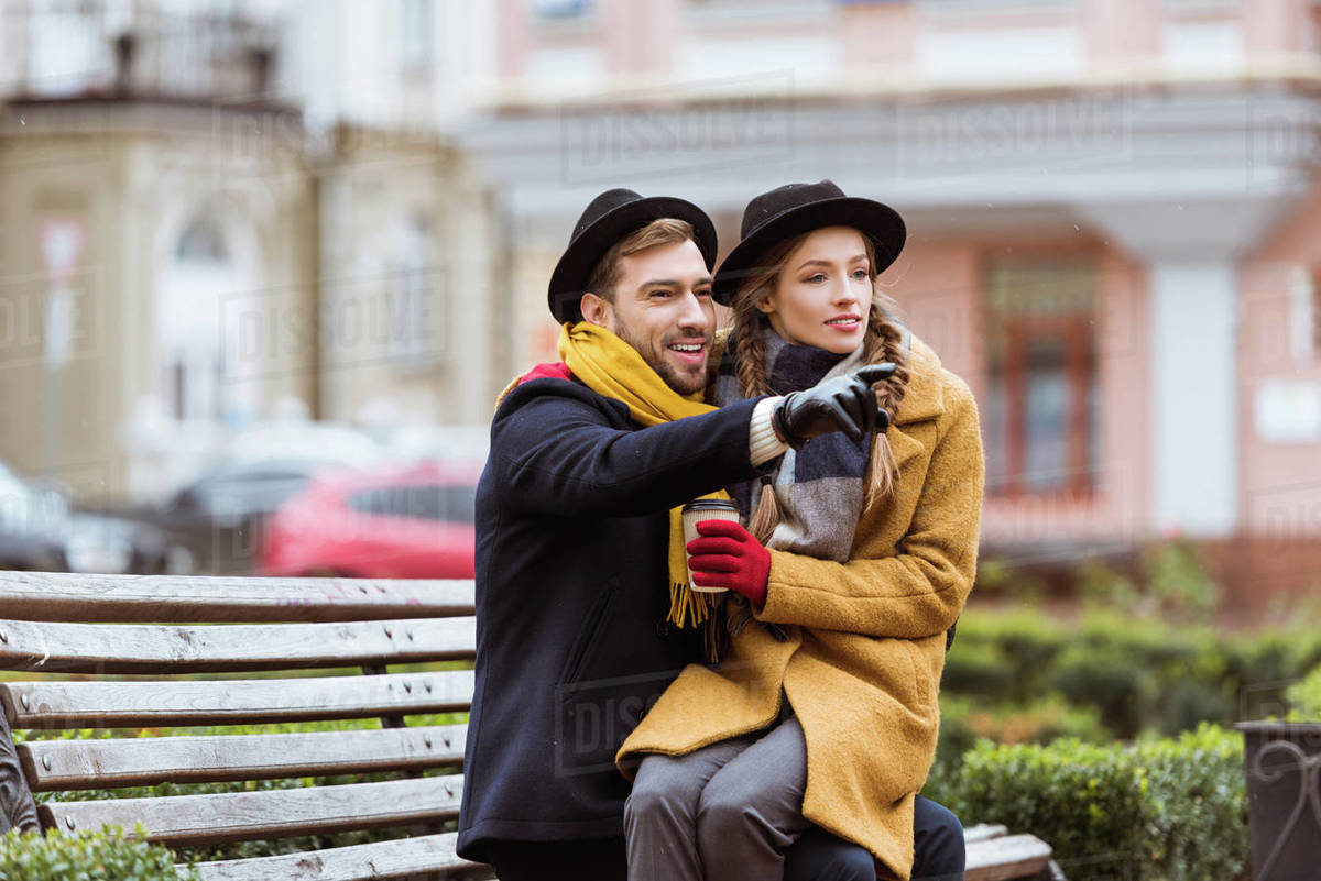 Happy couple sitting on bench and pointing on something - Royalty-free ...