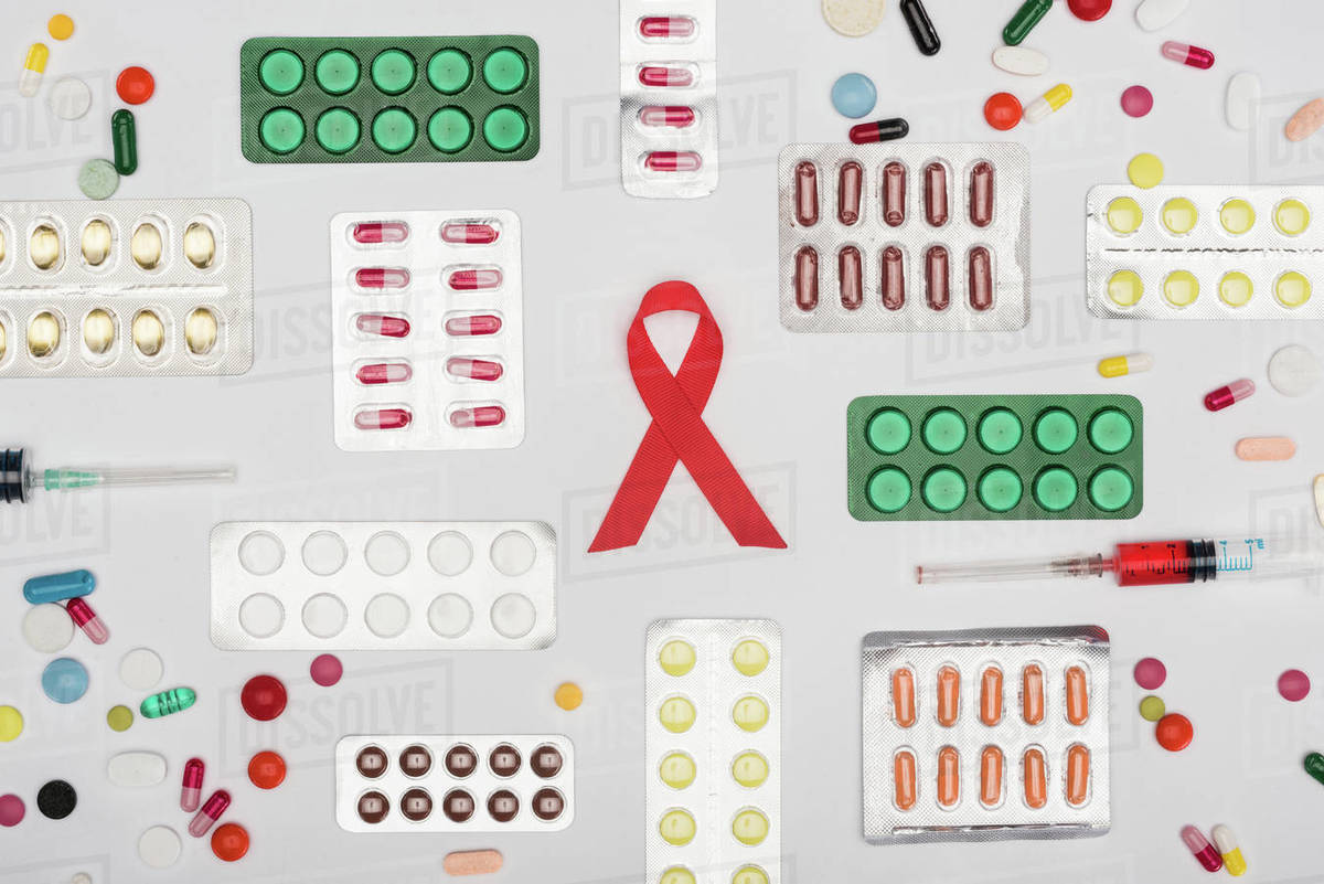 Top view of red aids ribbon in middle of different pills and syringes ...