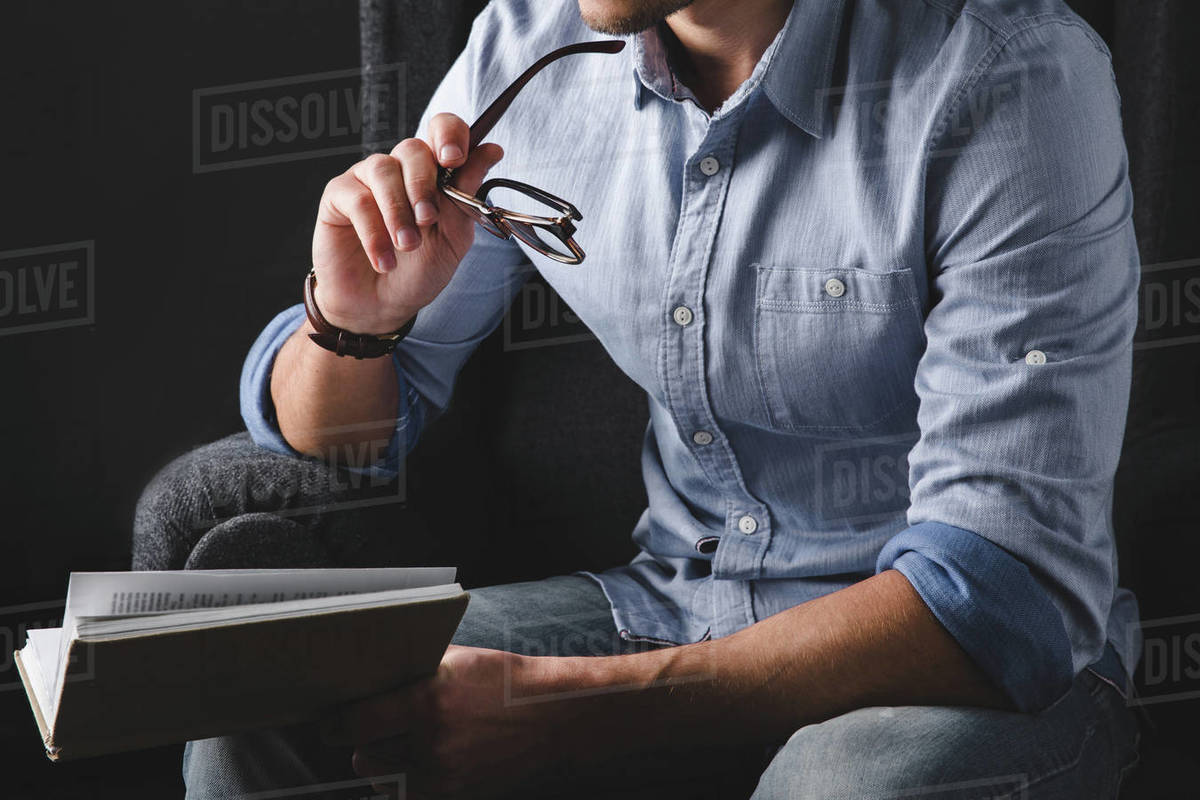 Cropped view of man holding eyeglasses while reading book - Royalty ...