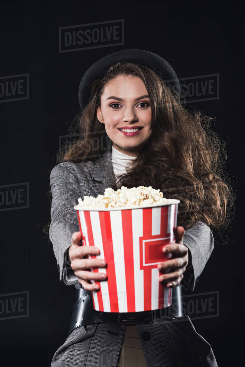 Beautiful elegant young woman holding popcorn and smiling at camera ...