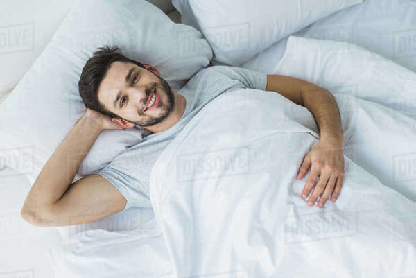 Top view of cheerful man lying on bed in the morning - Royalty-free ...