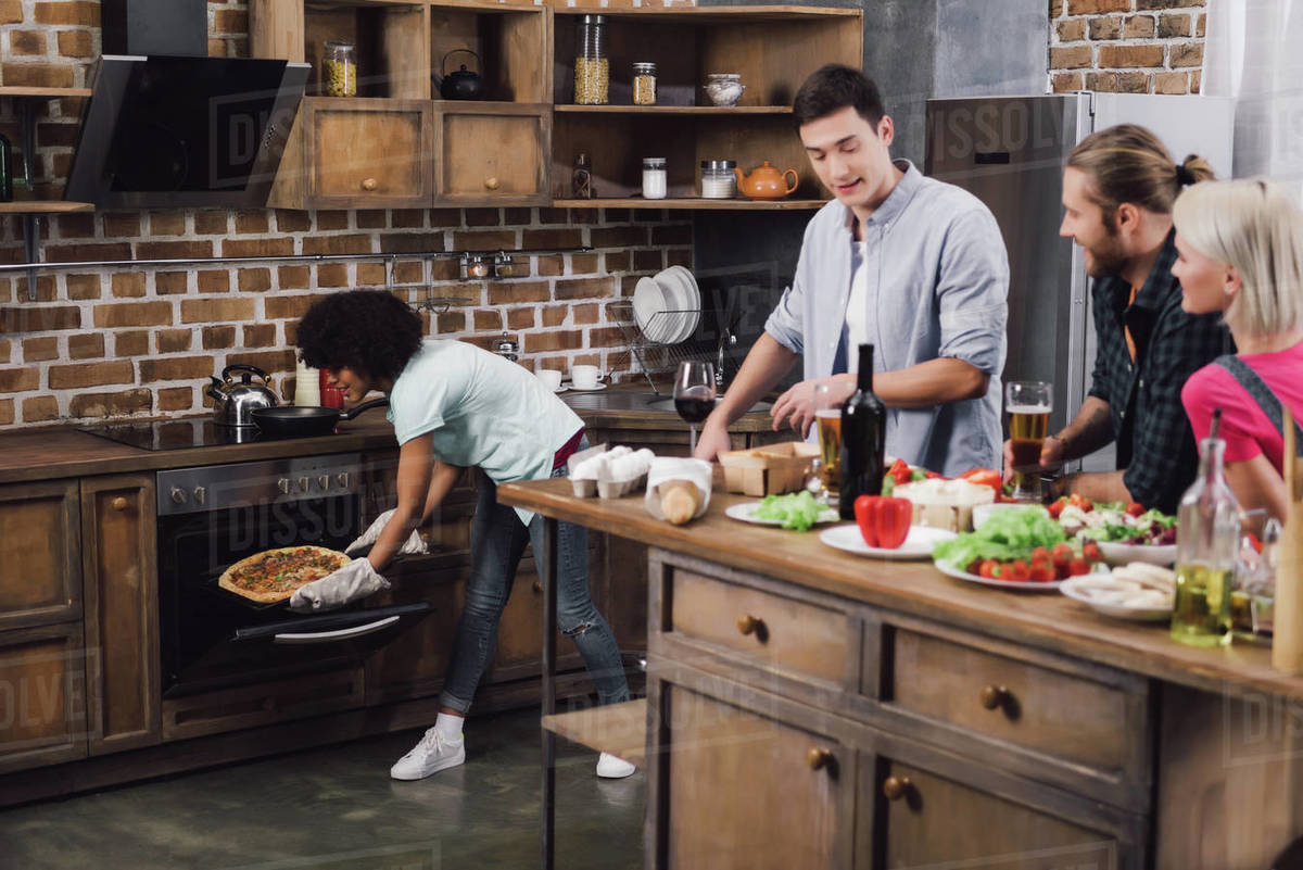 African American girl bringing homemade pizza to friends in kitchen ...