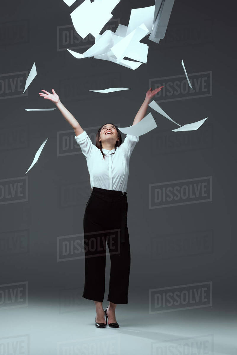 Full length view of happy young businesswoman throwing papers on grey ...