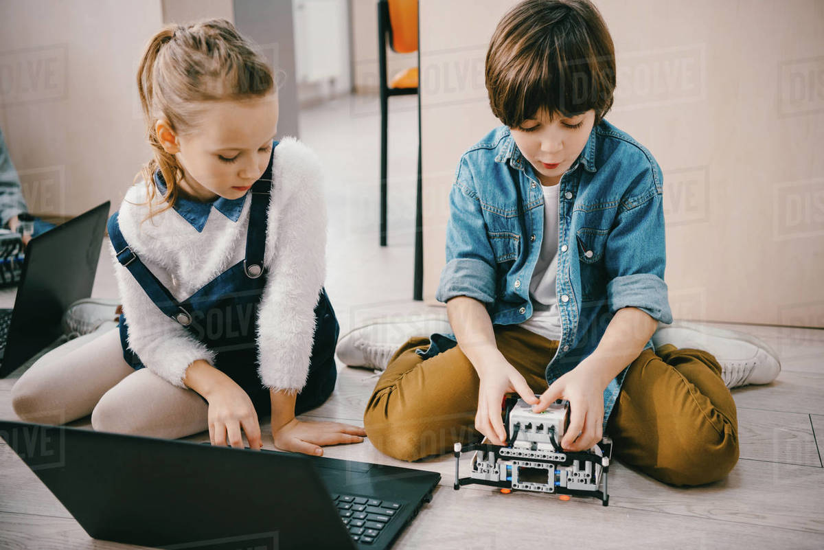 focused kids programming robot while sitting on floor at machinery ...