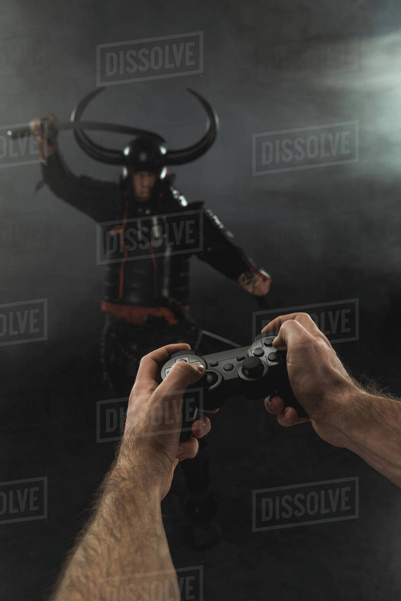 Cropped shot of man controlling samurai character with gamepad on black ...