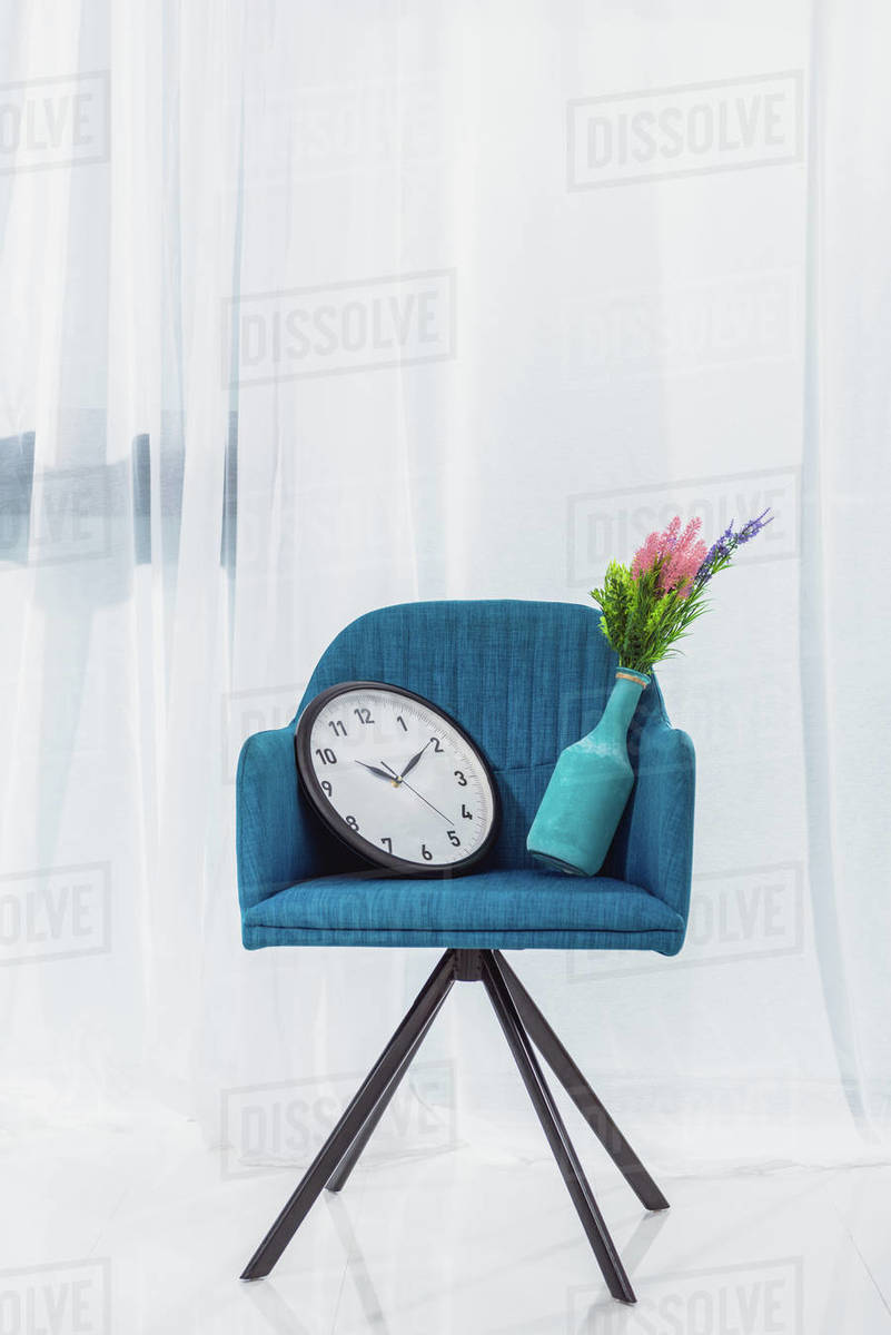 Vase and clock in blue modern chair in room in front of window - Stock ...