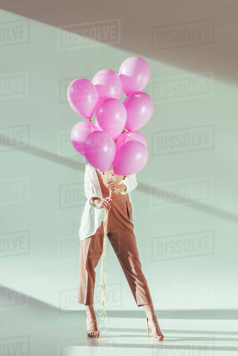 Stylish young woman hiding behind pink balloons on grey - Royalty-free ...