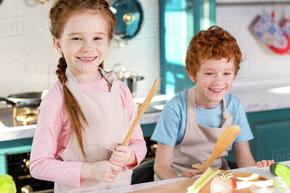 Adorable kids in aprons laughing while cooking together in kitchen ...
