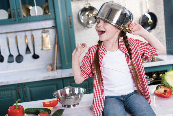 Happy little child with pan on head sitting on kitchen table - Stock ...