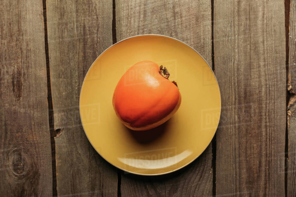 top view of persimmon on yellow plate on wooden table - Royalty-free ...