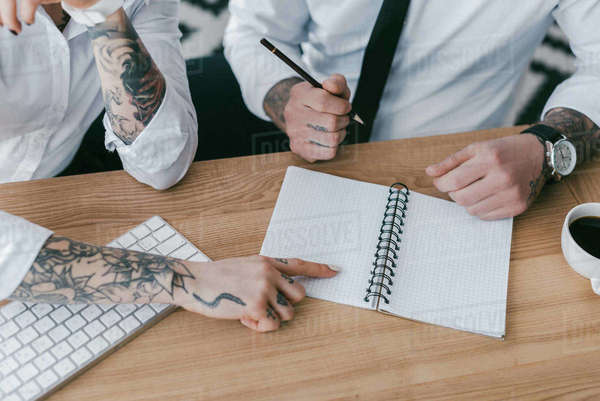 Cropped shot of young business people with tattoos taking notes ...