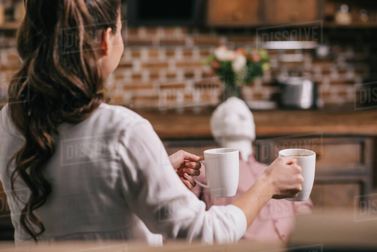 Back view of woman serving coffee to manikin at home, perfect ...