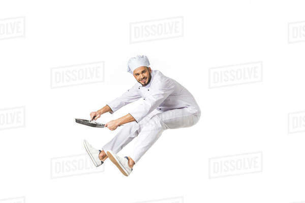 Happy young chef with frying pan jumping and looking at camera isolated ...