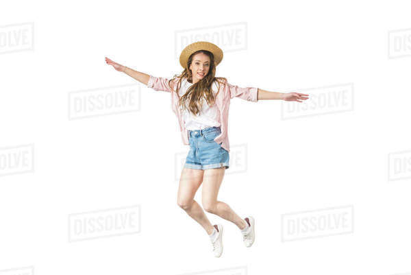 Happy girl in hat jumping with open arms and smiling at camera isolated ...